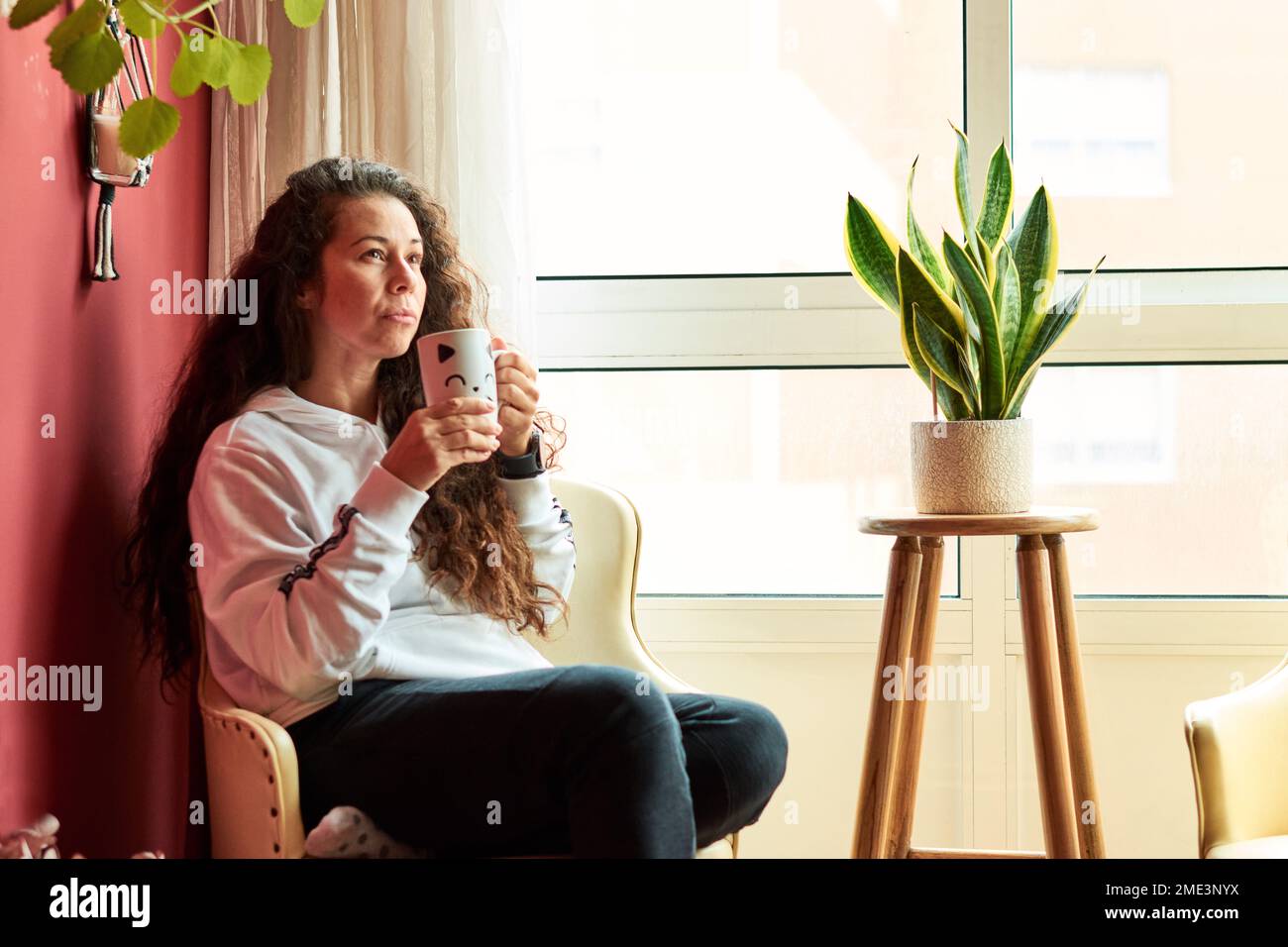 Woman relaxing in a armchair drinking a cup of tea indoors surrounded ...