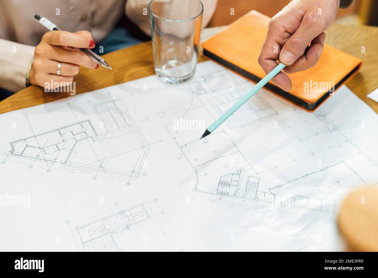 Hand of businessman pointing with pen on blueprint by colleague at ...
