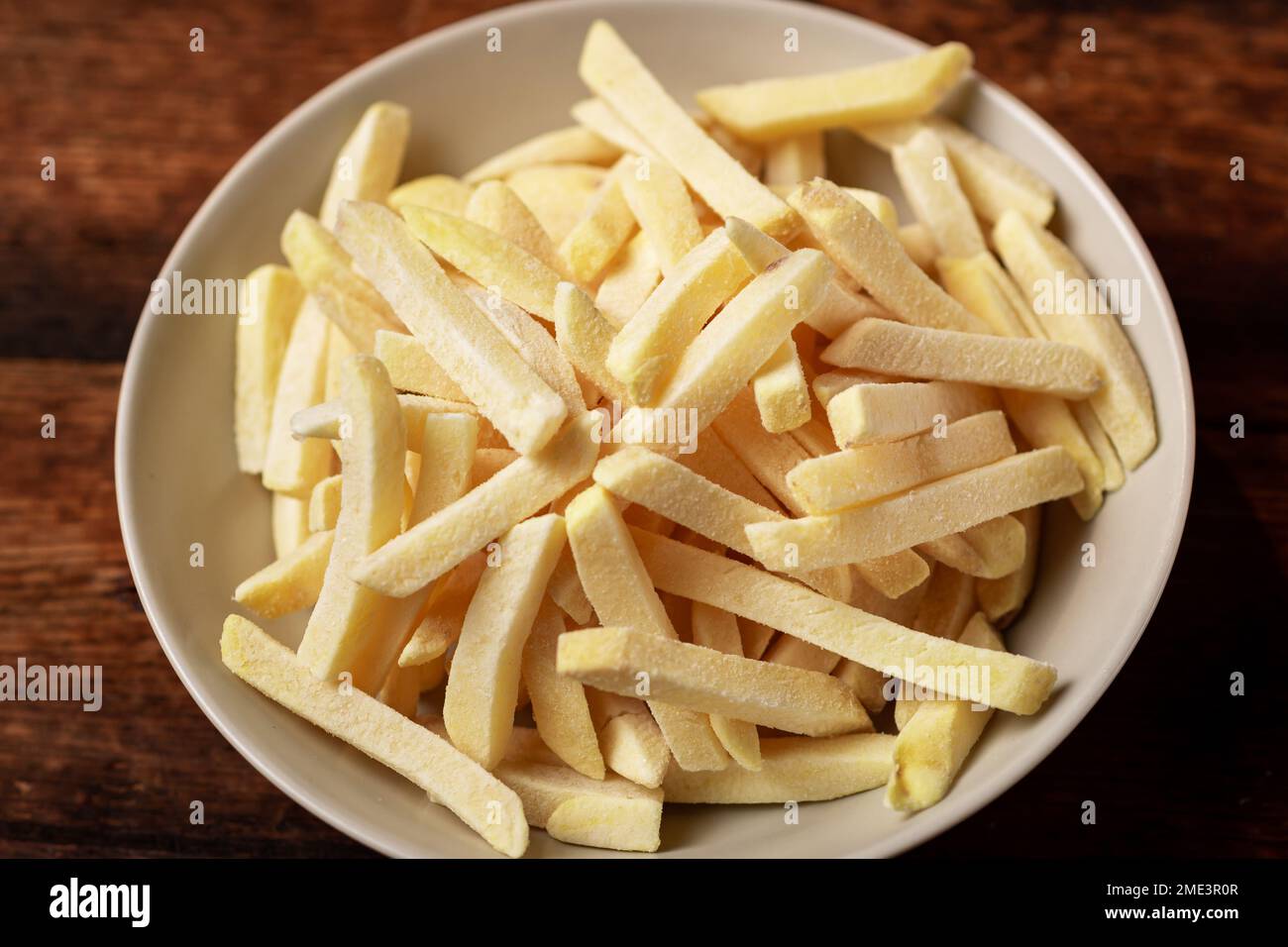 Frozen french fries on a plate on a wooden background. Semi-finished ...