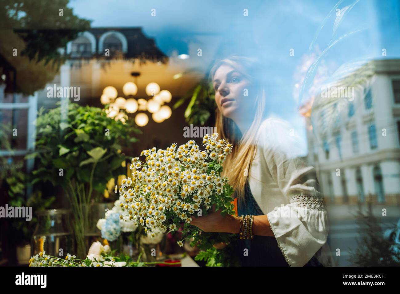 Thoughtful florist with bouquet of daisy flowers seen through glass ...