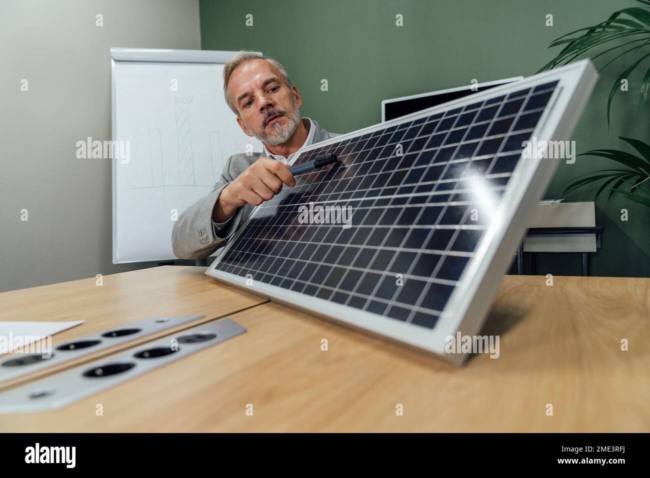 Mature businessman with solar panel sitting at conference table Stock ...