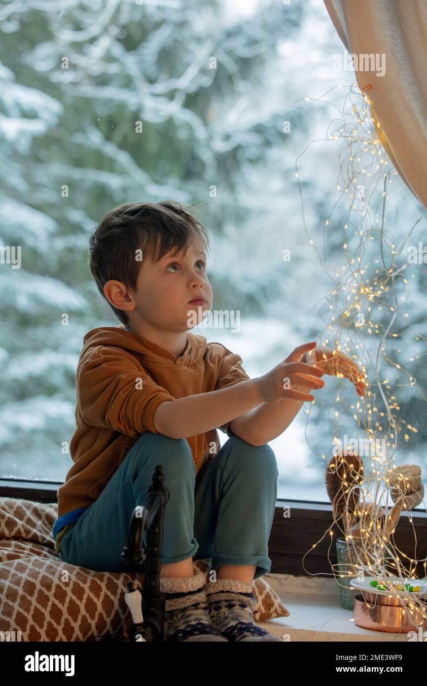 Boy touching string lights sitting on window sill at home Stock Photo ...