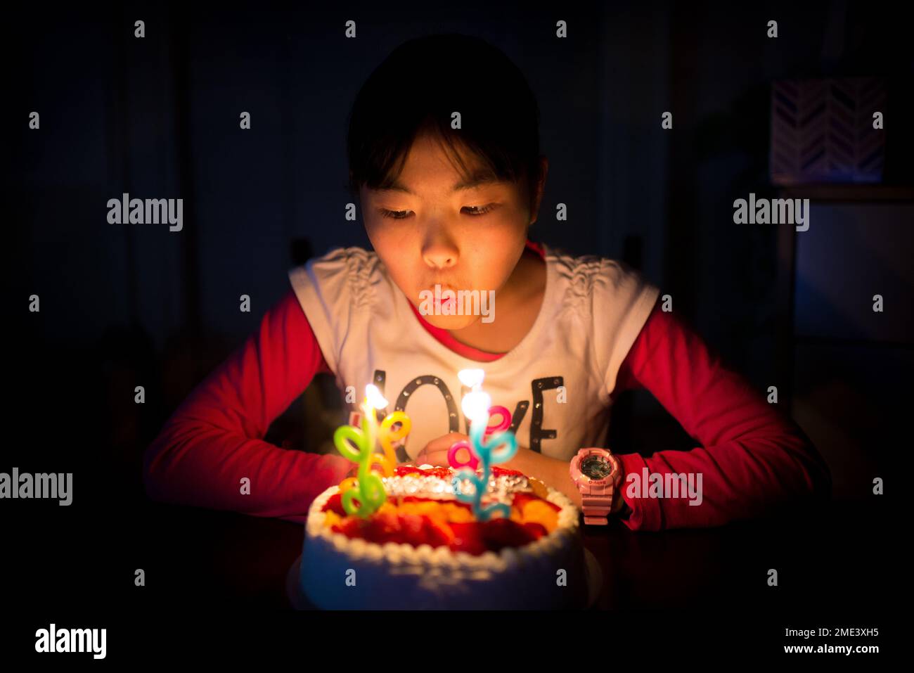 Young asian girl sitting in dark in front of her birthday cake before ...