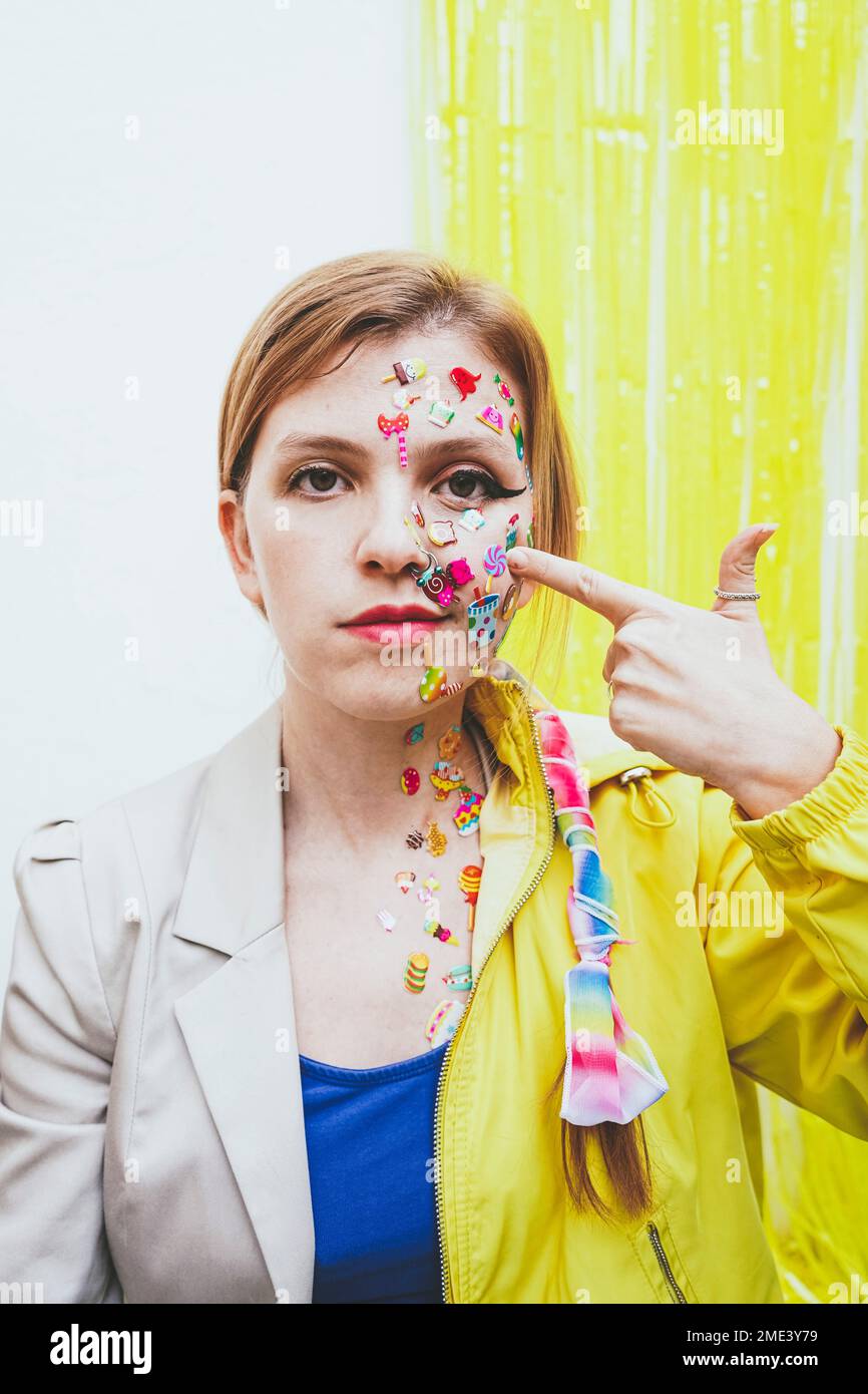 Woman pointing at stickers on face in front of two tone wall Stock ...