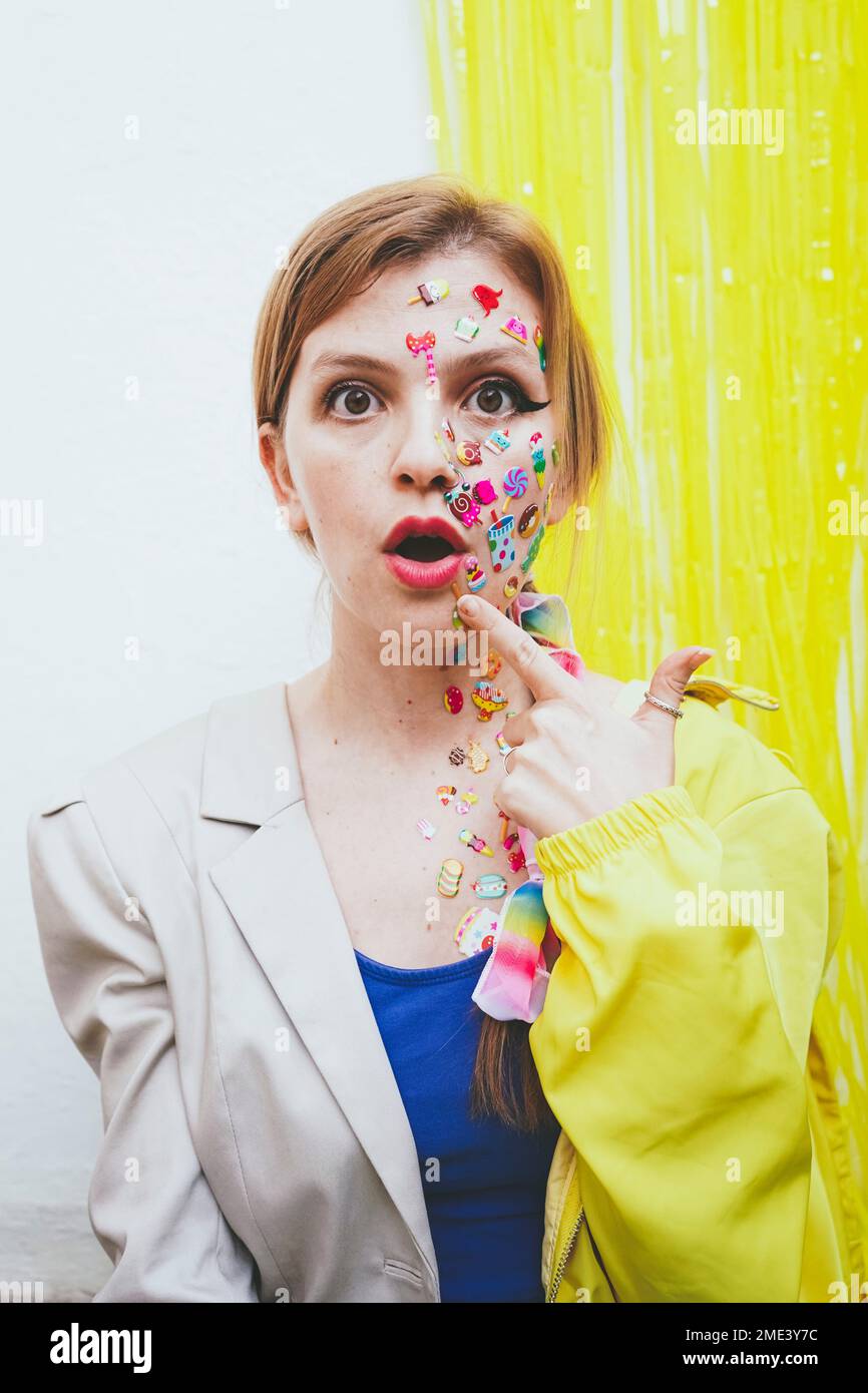 Surprised woman with stickers on face gesturing in front of two tone ...