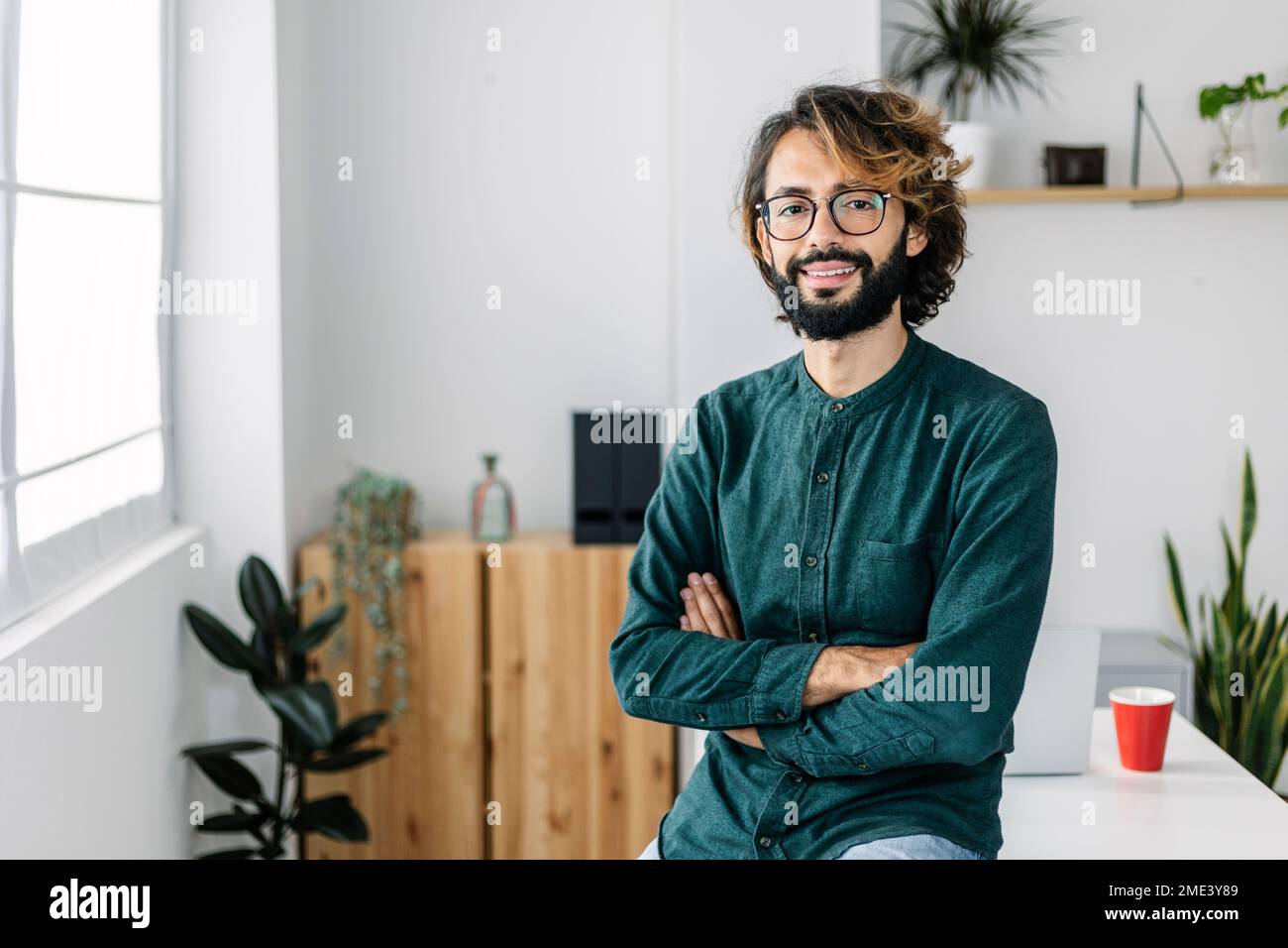 Happy freelancer with arms crossed sitting on desk Stock Photo - Alamy