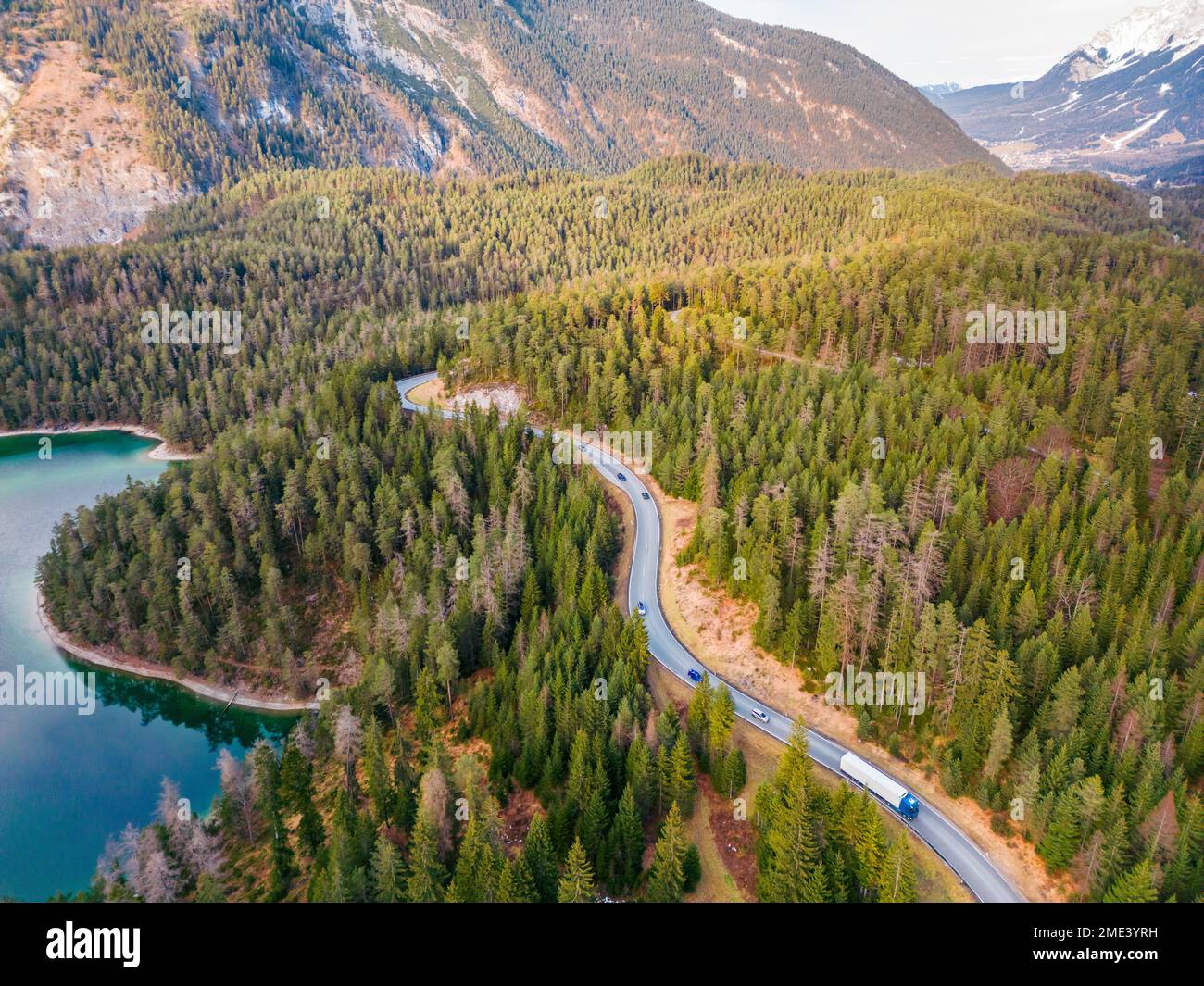An aerial view of a lake surrounded by trees beside a road, and a ...