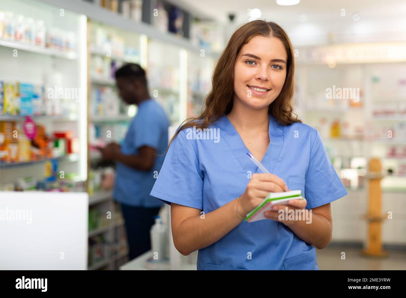 Young smiling female pharmacist making important notes in a notebook ...