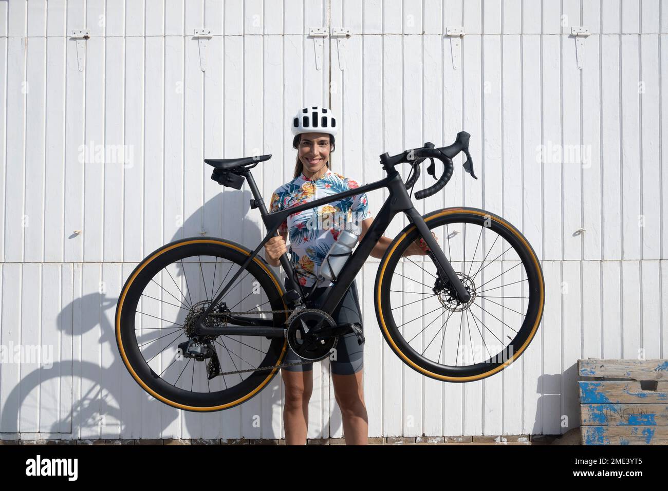 Happy cyclist lifting bicycle in front of white wall Stock Photo - Alamy
