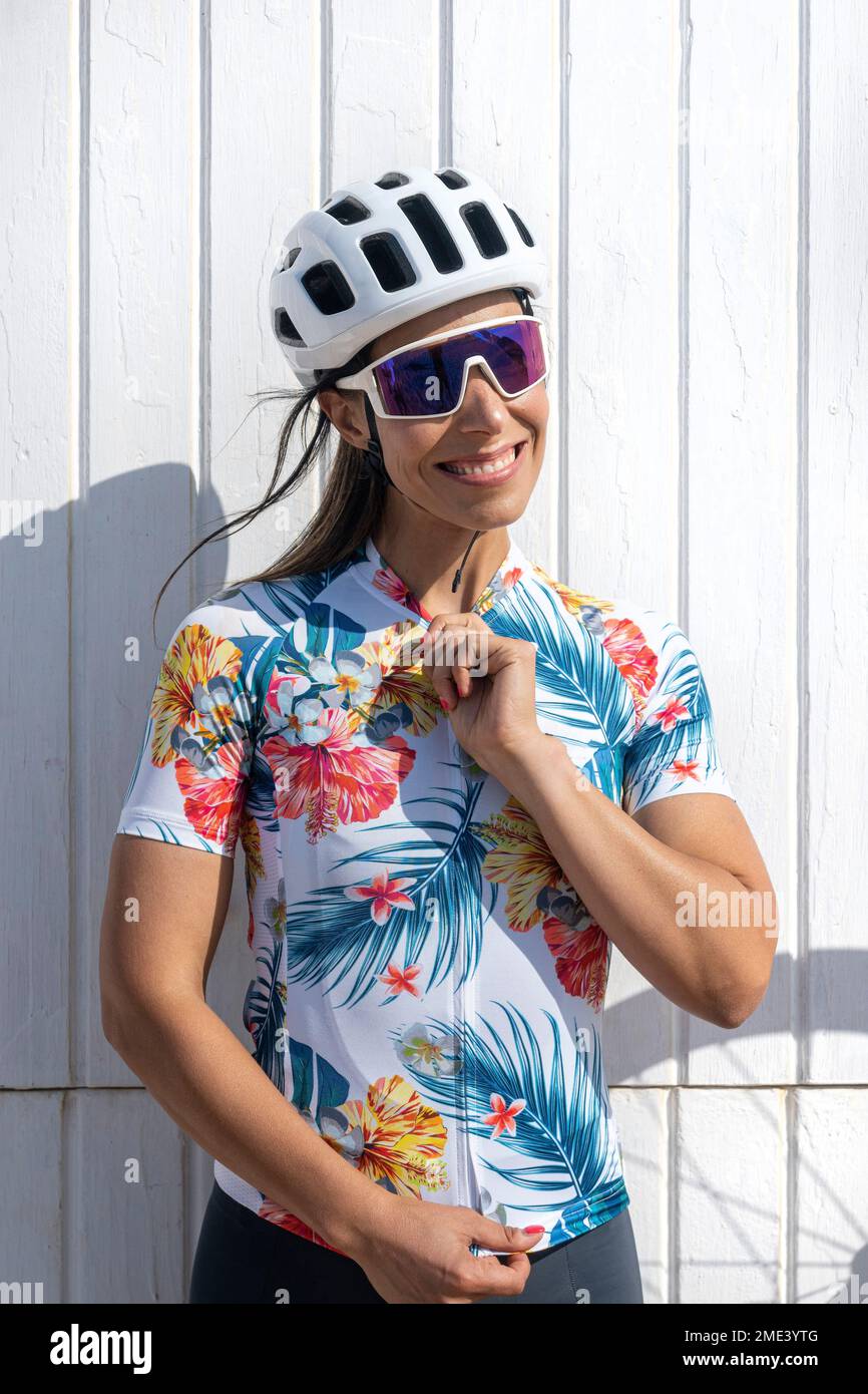Happy cyclist wearing sunglasses and helmet standing in front of wall ...