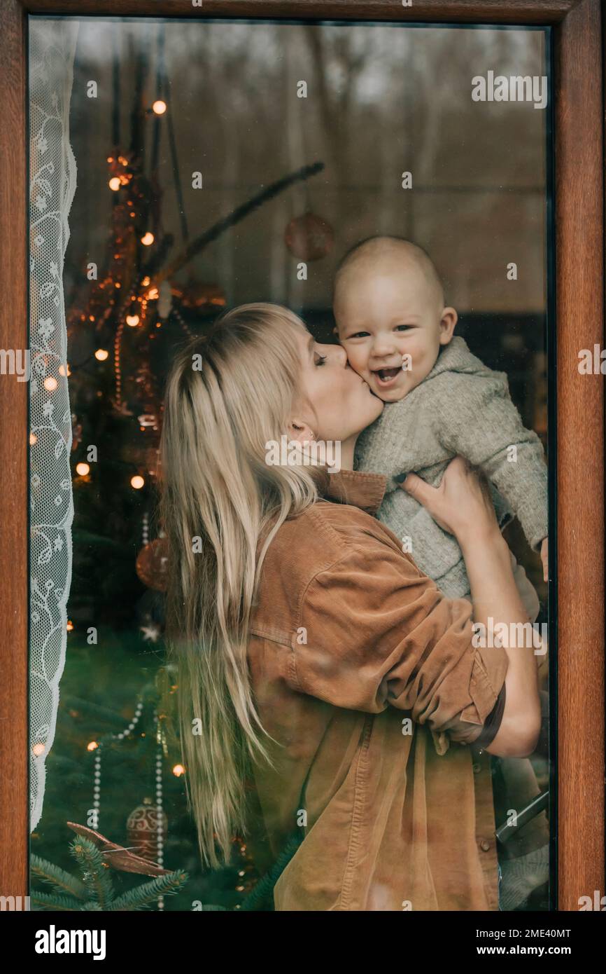 Mother kissing baby boy seen through window at home Stock Photo - Alamy