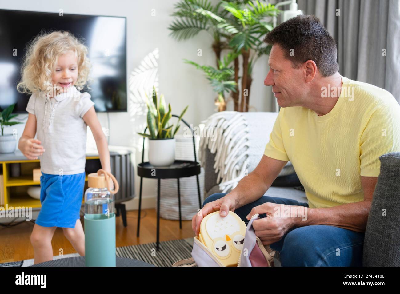 Father putting lunch box in bag and looking at daughter in living room ...