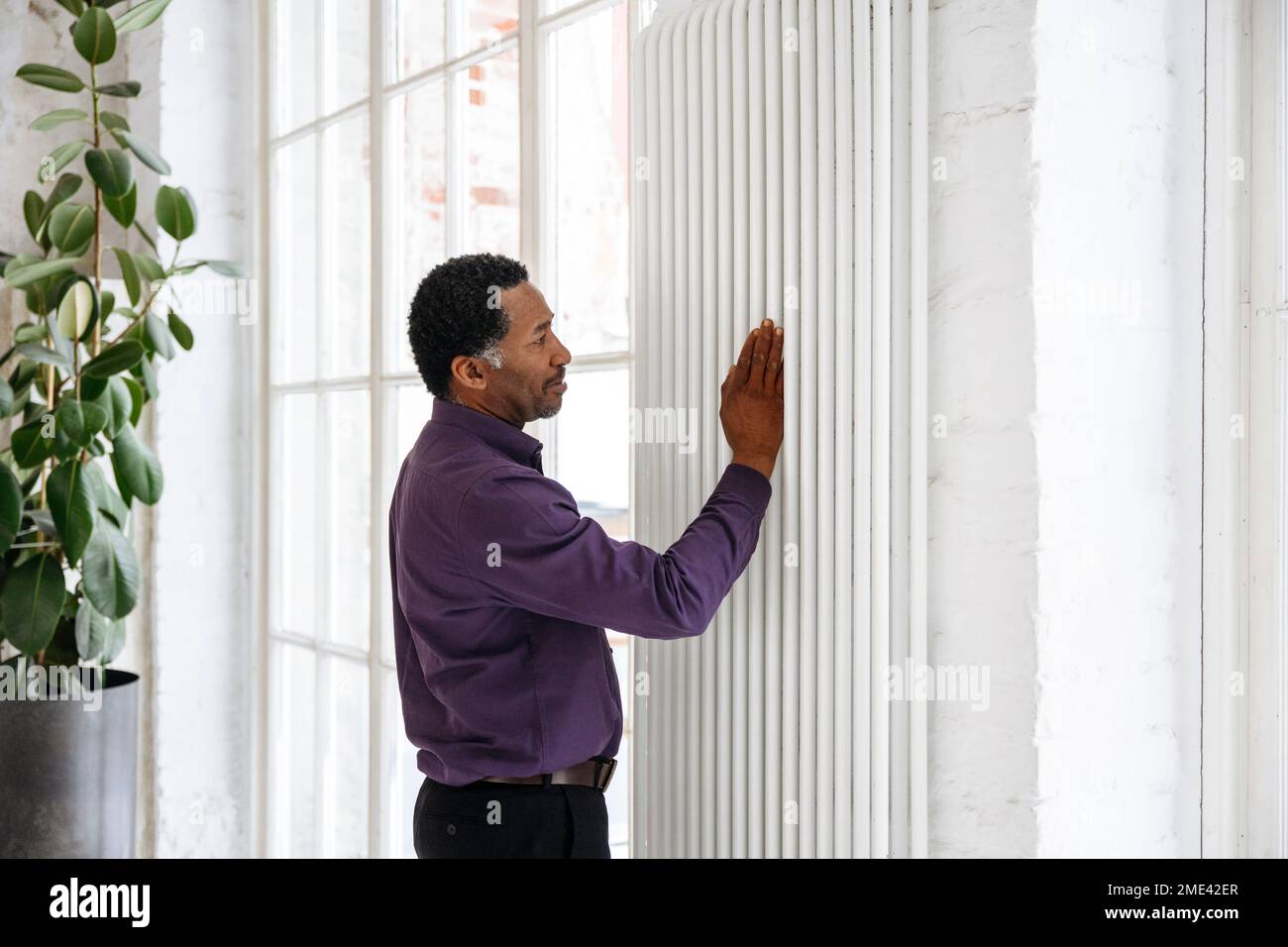 Mature man touching radiator at the window Stock Photo - Alamy