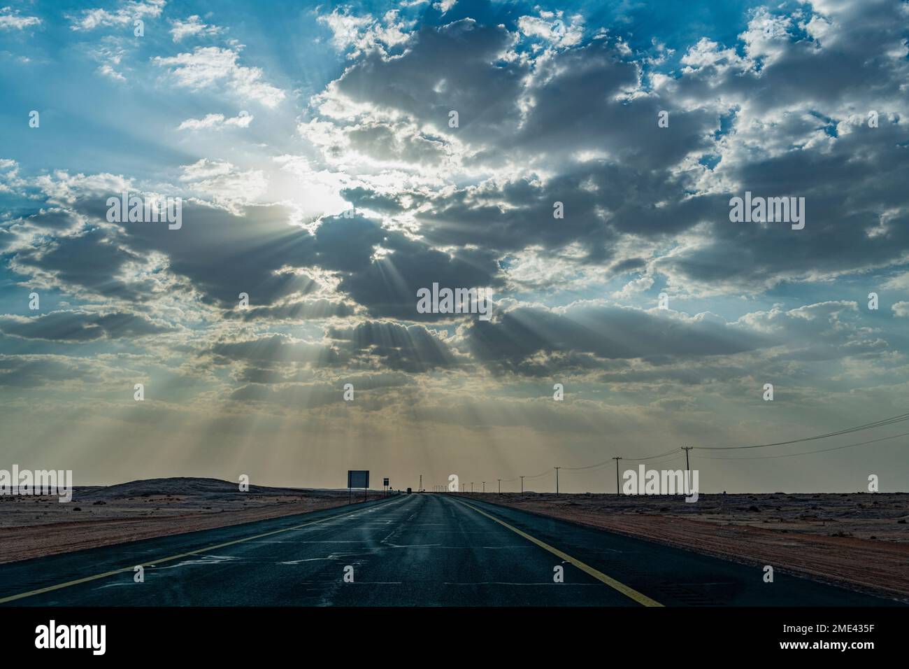 Saudi Arabia, Al-Ula, Setting sun piercing clouds over empty highway ...
