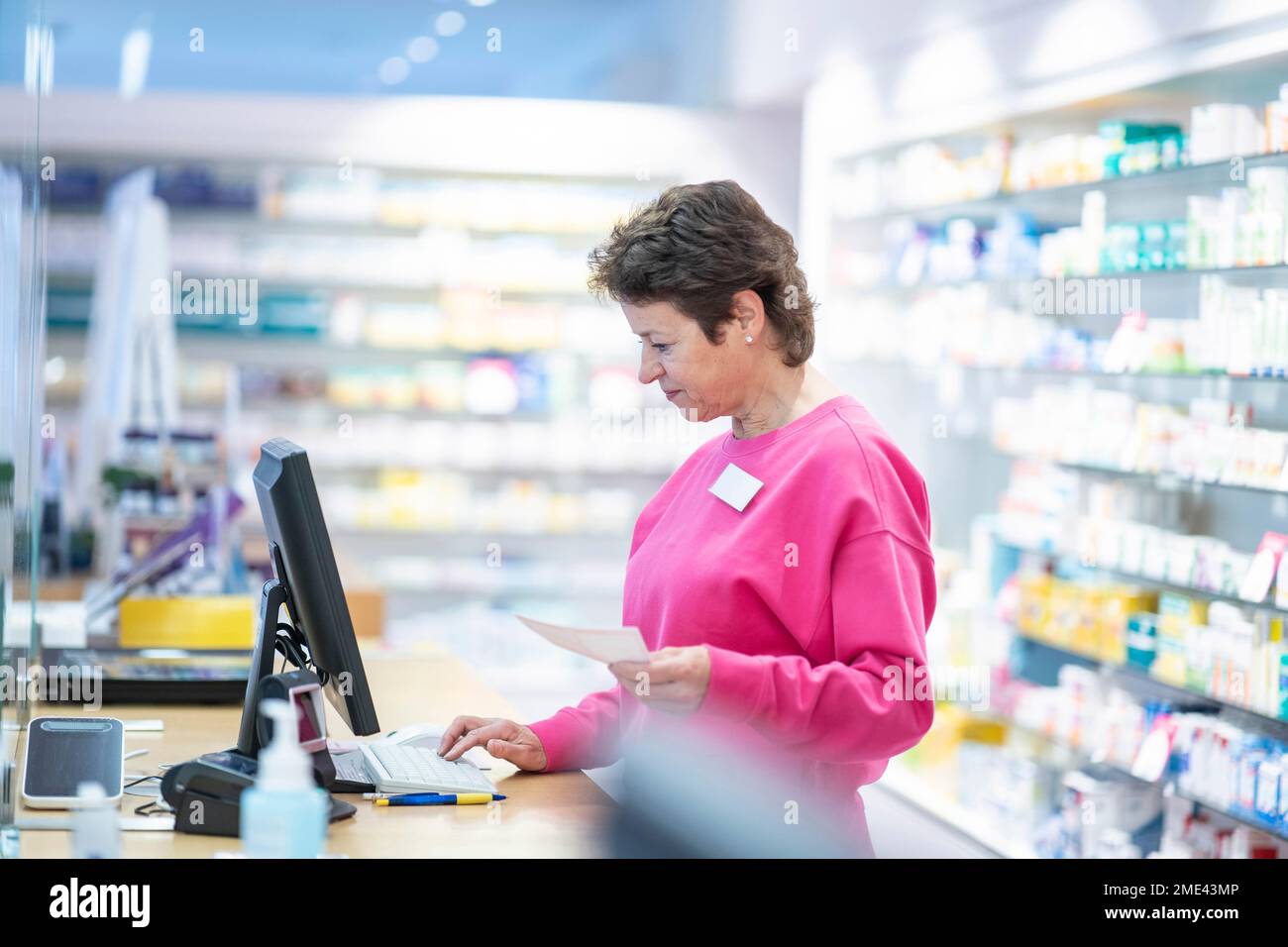 Smiling pharmacist with medical prescription using computer at desk ...