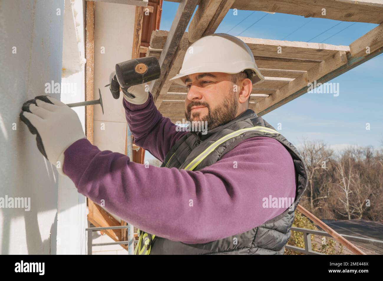 Construction worker using hammer on wall to install polystyrene foam ...