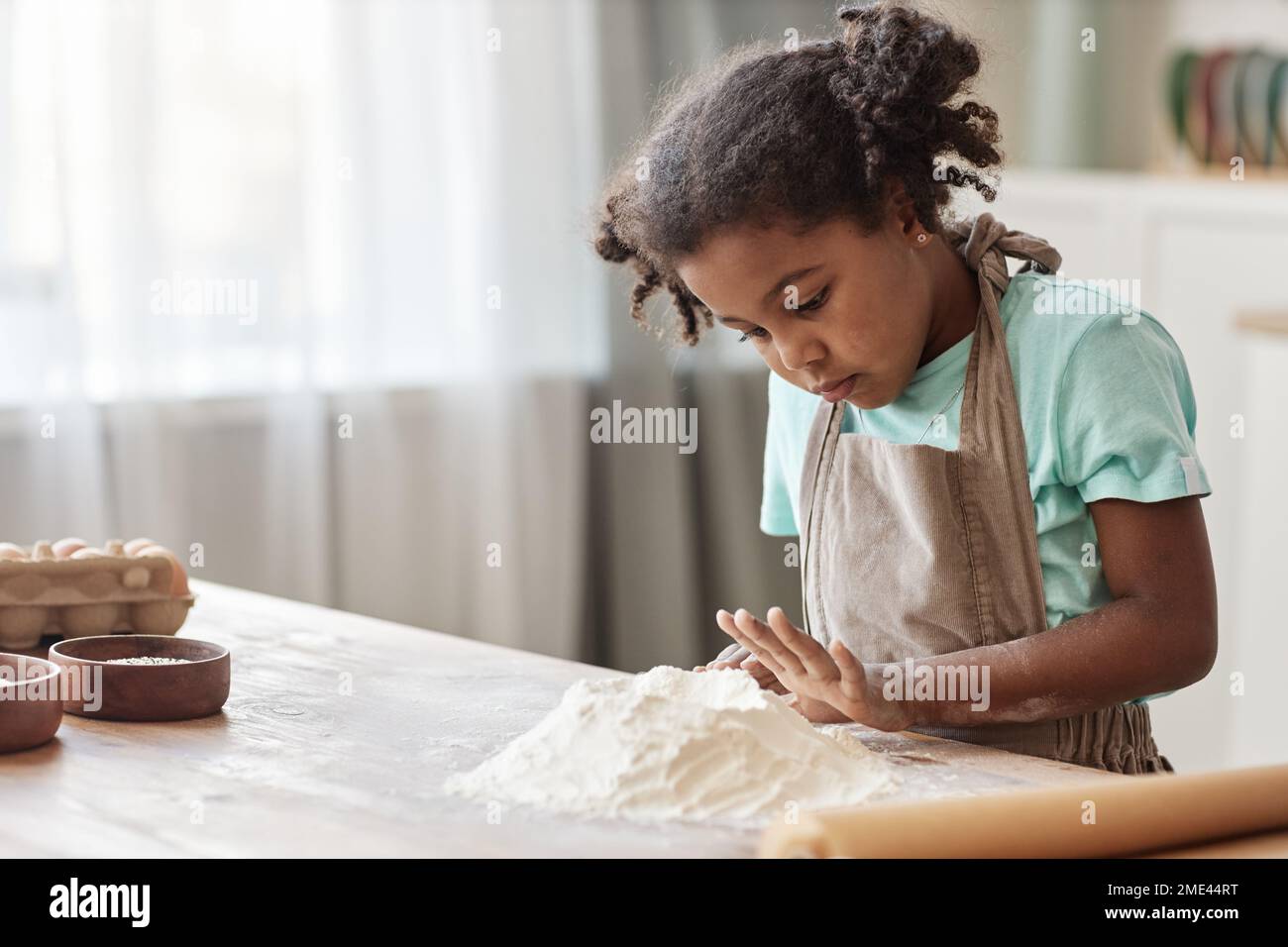 Candid minimal portrait of cute black girl baking in kitchen and ...