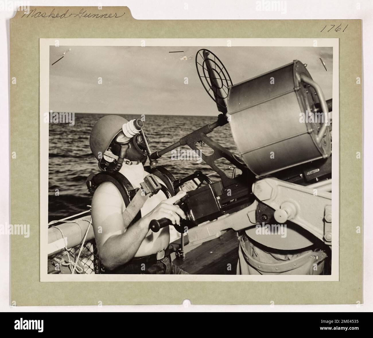 A Coast Guard gunner wears a helmet and gas mask while tracking a plane ...
