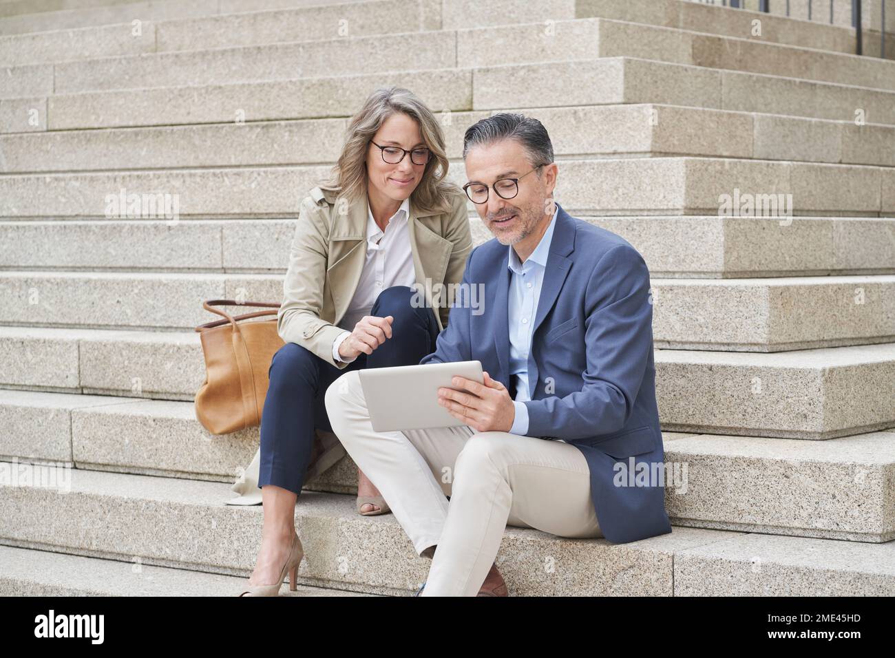 Mature businessman using tablet PC sitting by colleague on steps Stock ...