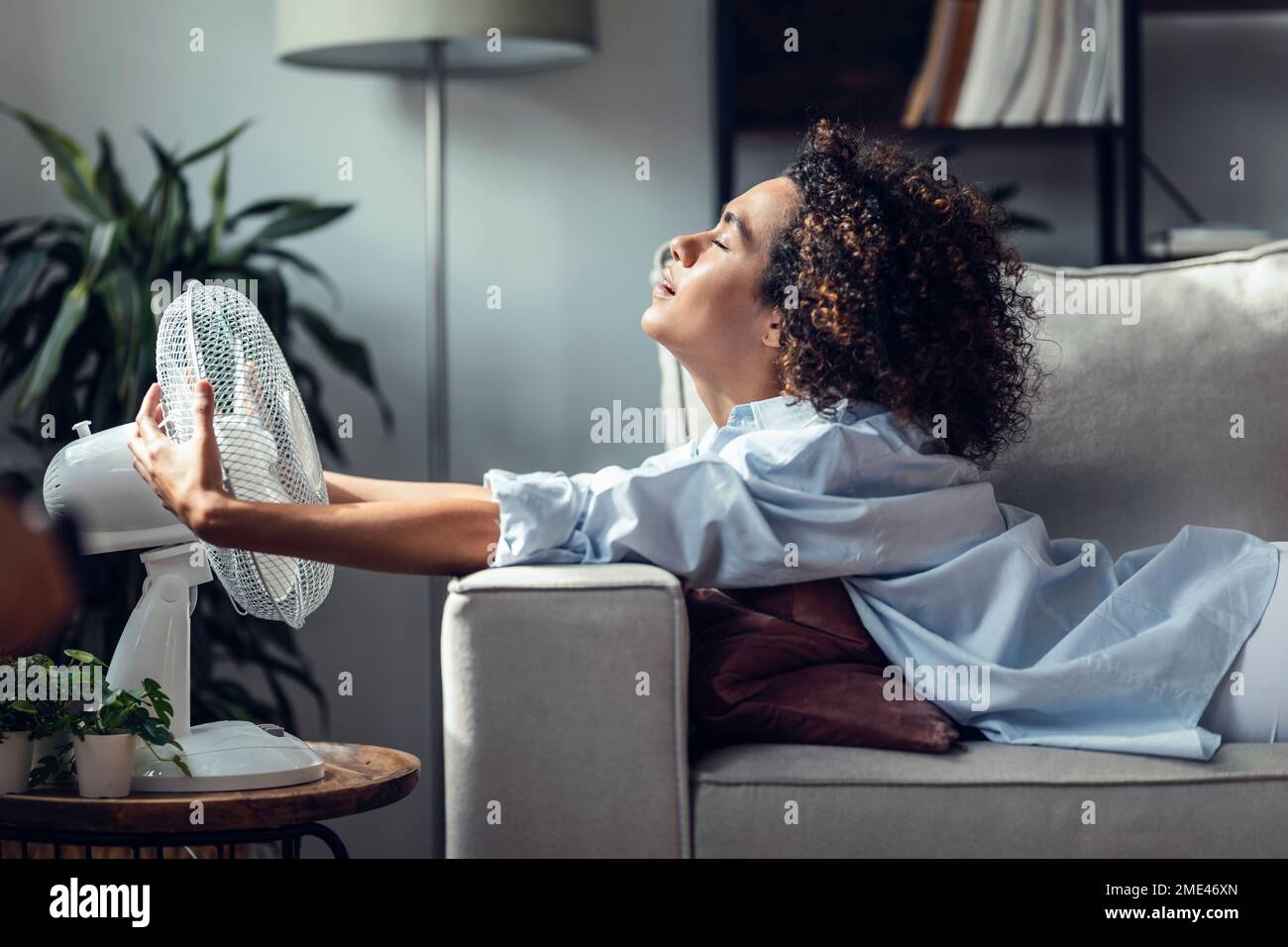 Woman cooling off using electric fan lying on sofa at home Stock Photo ...