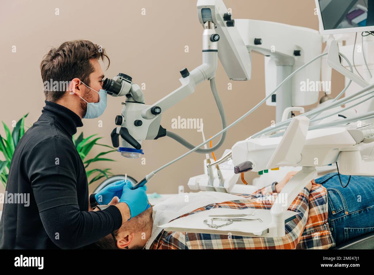 Young dentist examining patient's teeth through microscope in clinic ...