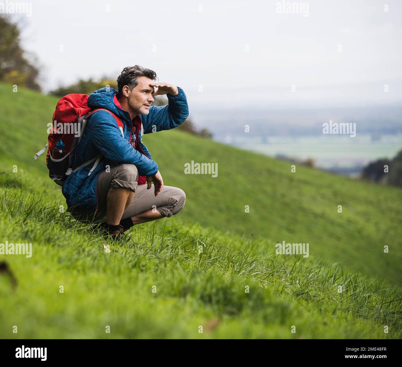 Mature man shielding eyes and crouching on meadow Stock Photo - Alamy