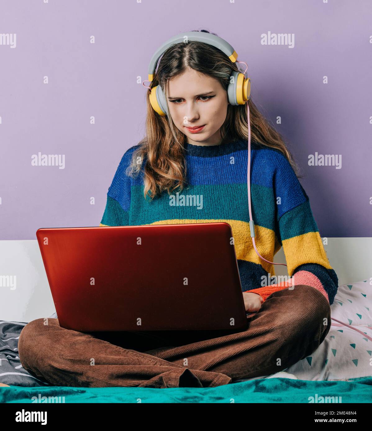 Girl wearing headphones doing home work using laptop in front of purple ...