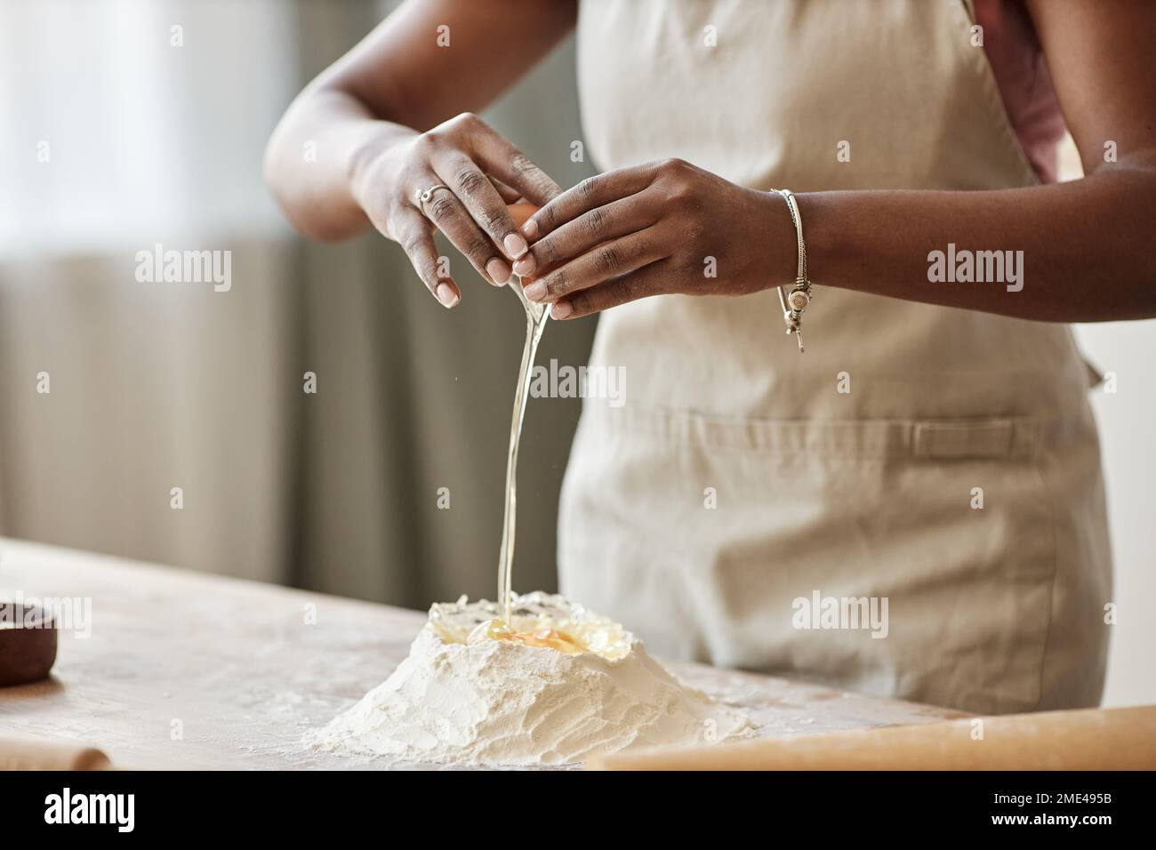 Closeup of black woman baking in kitchen and breaking eggs and mixing with flour while making ...