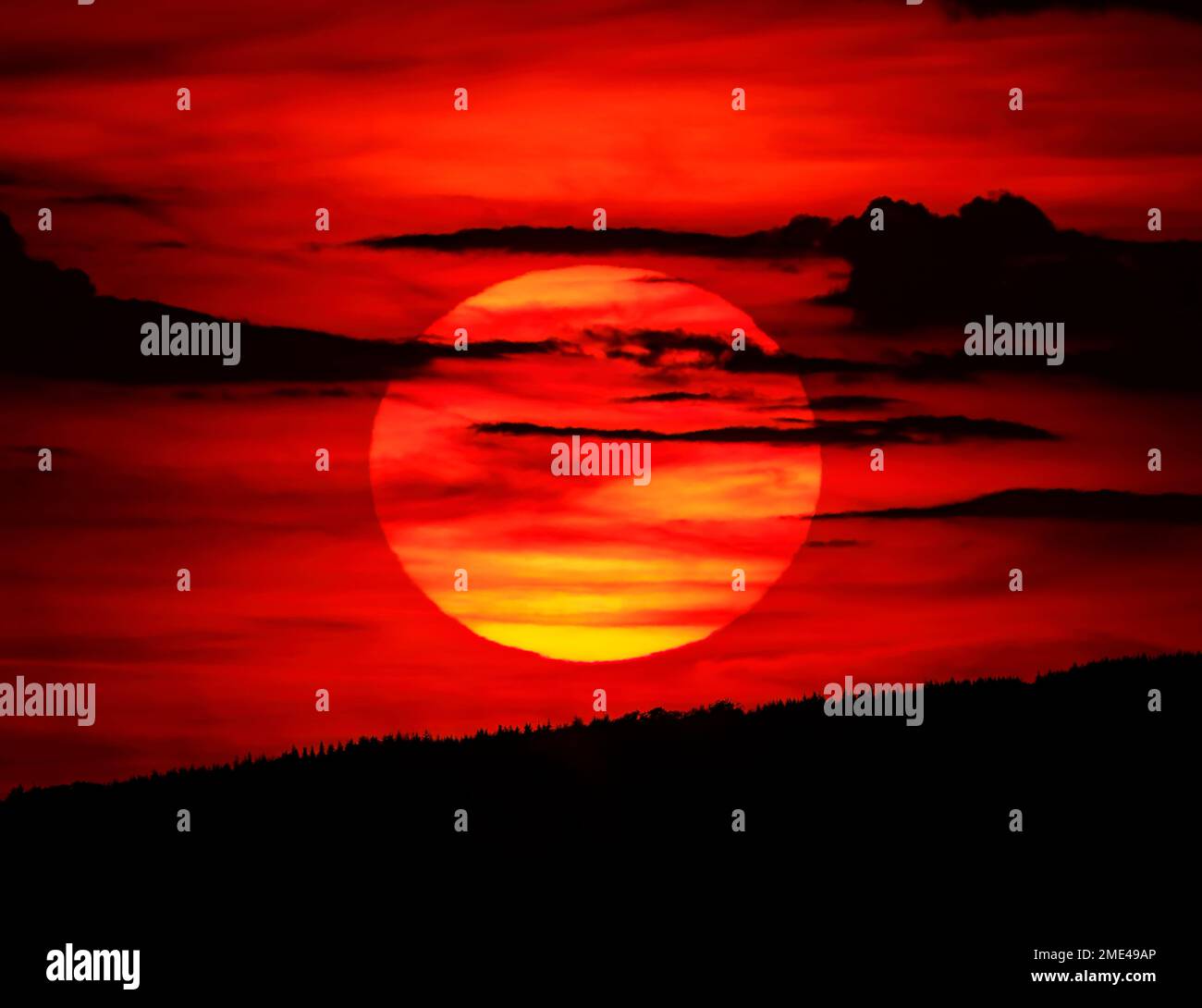 Sun setting against fiery red sky Stock Photo - Alamy