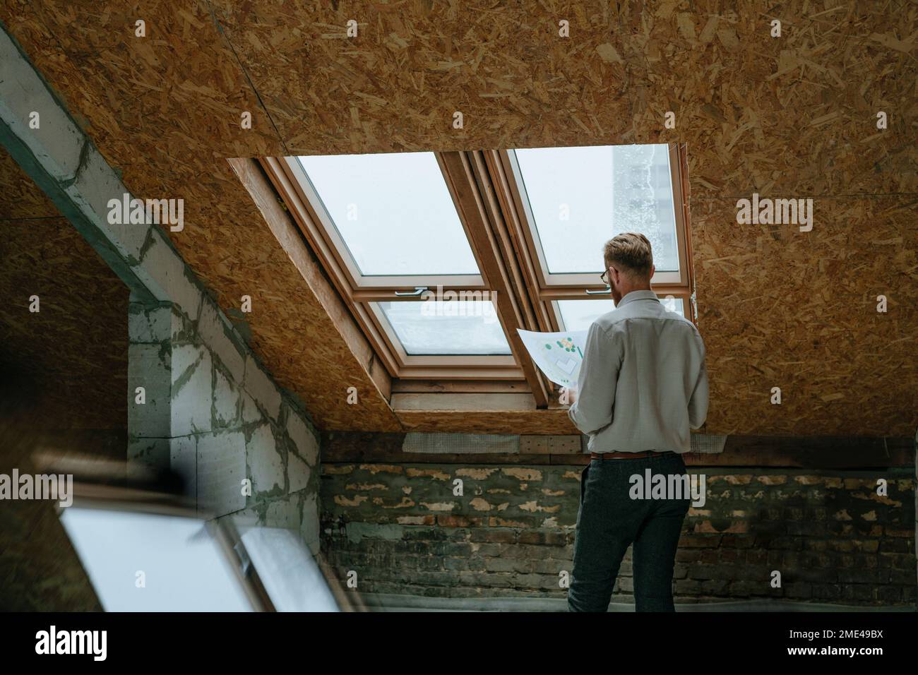 Architect looking at blueprint standing near window at construction ...