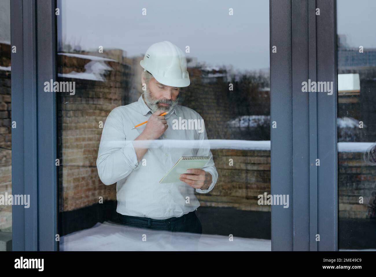 Architect wearing hardhat making notes seen through window Stock Photo ...