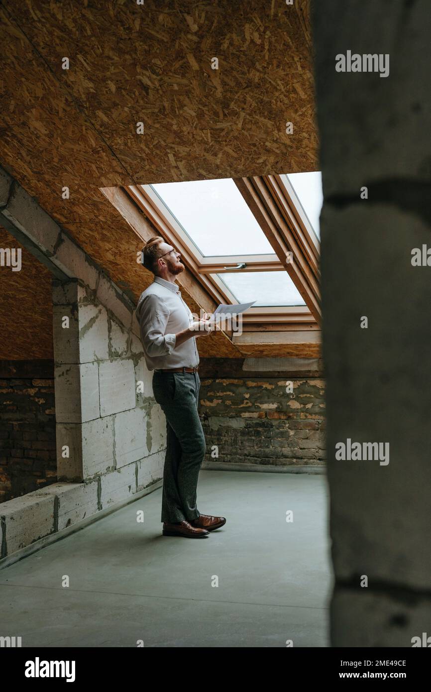 Architect with blueprint looking through window at construction site ...