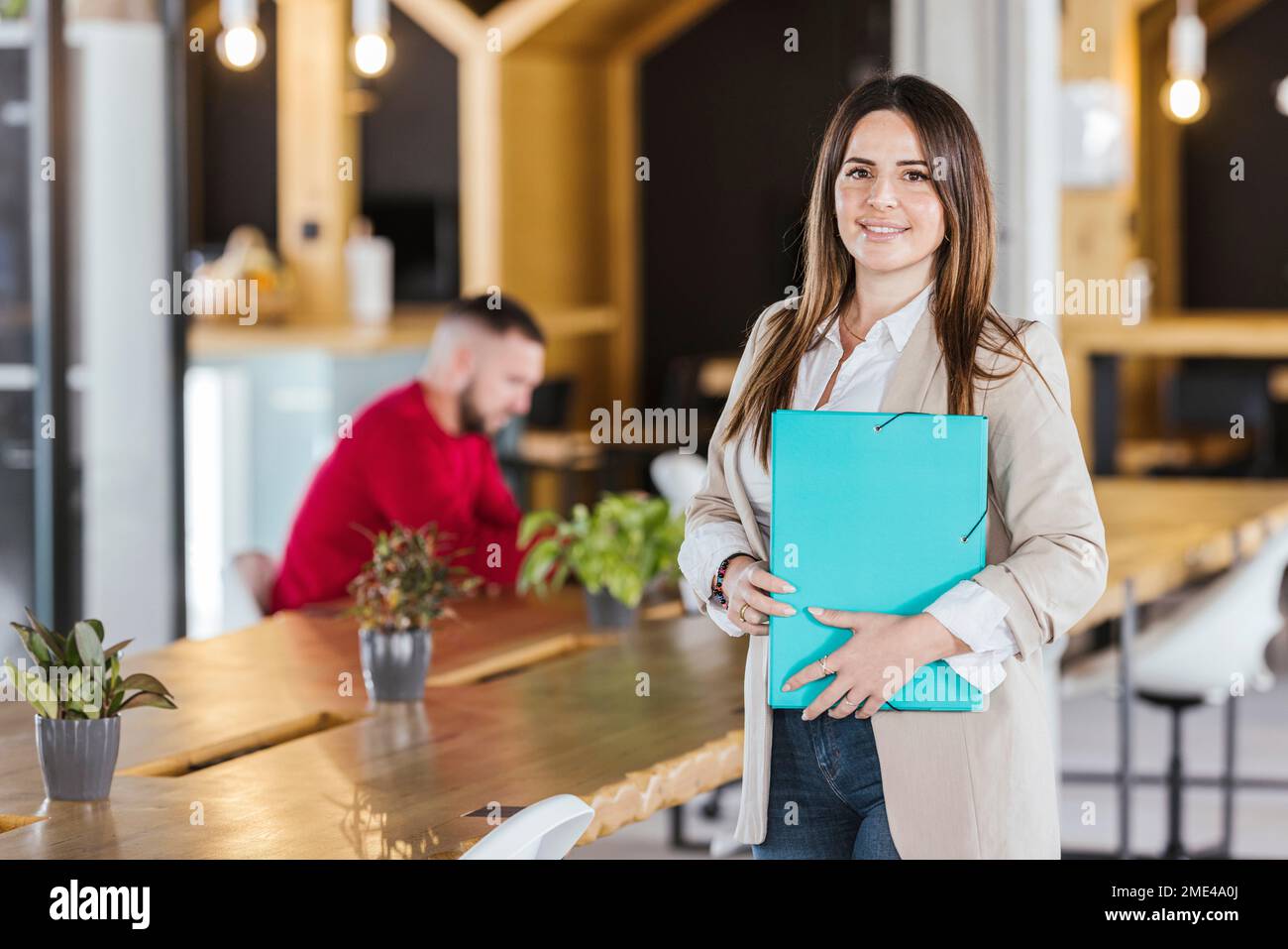 Smiling businesswoman with file folder standing by desk in office Stock ...