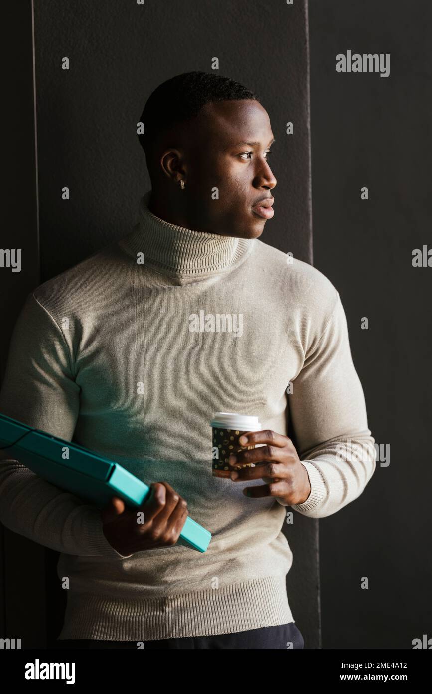 Businessman with coffee cup and file folder standing in front of wall ...