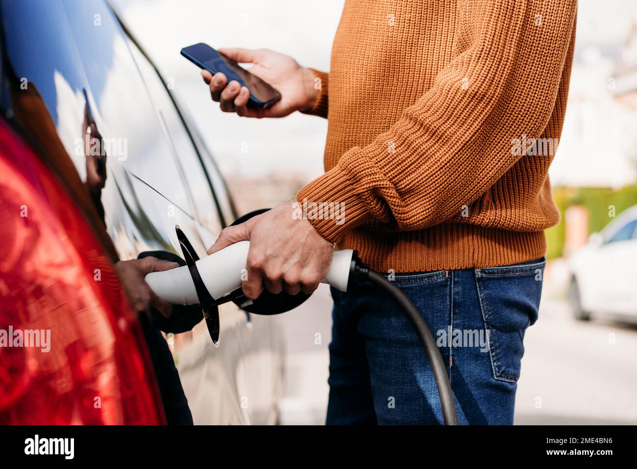 Man with smart phone plugging in electric plug at vehicle charging ...