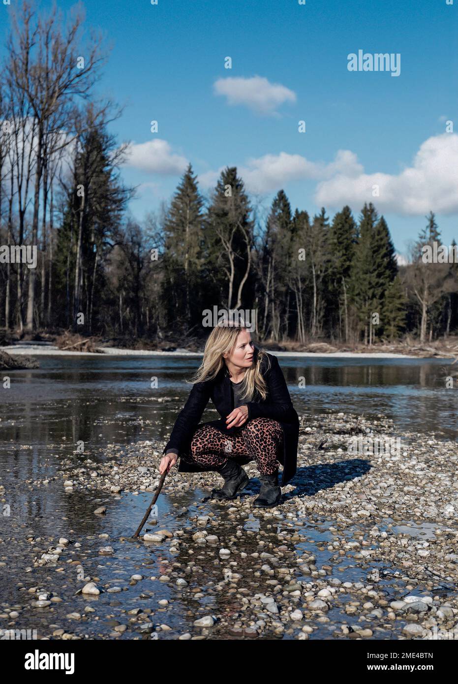 Mature woman playing with stick crouching at riverbank Stock Photo - Alamy