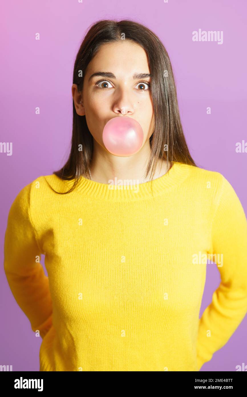 Surprised woman blowing bubble gum standing against purple background ...