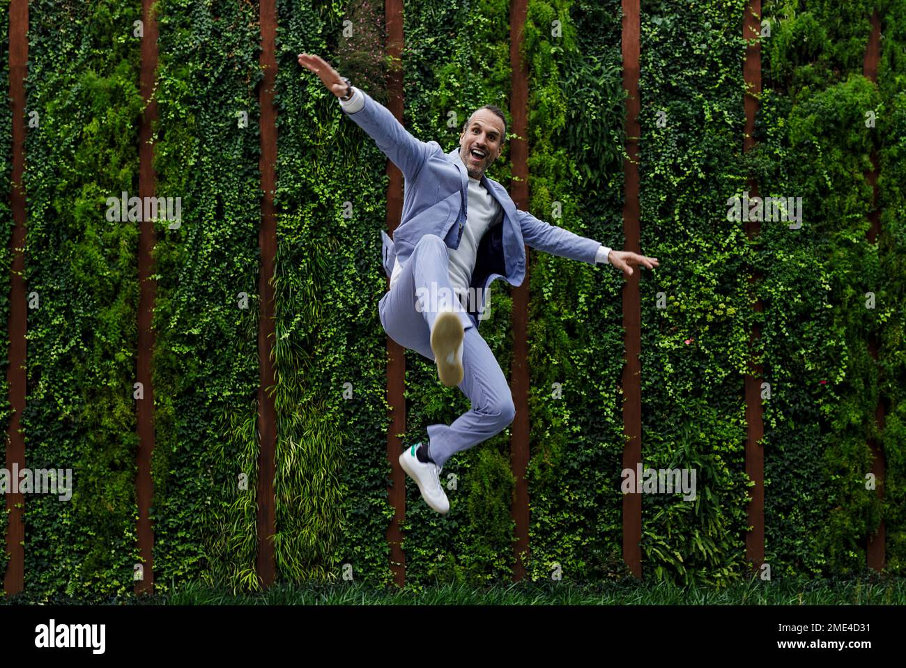 Happy man jumping with arms outstretched in front of hedge Stock Photo ...
