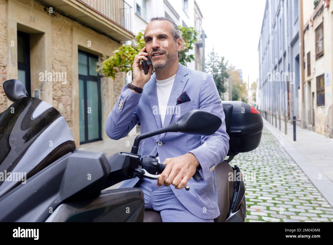 Mature businessman talking over mobile phone sitting on motorcycle ...