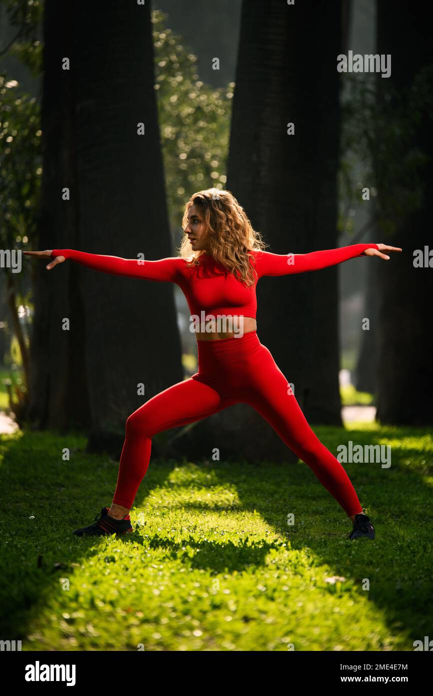 Woman with red colored yoga dress, posing yoga movements on a green ...