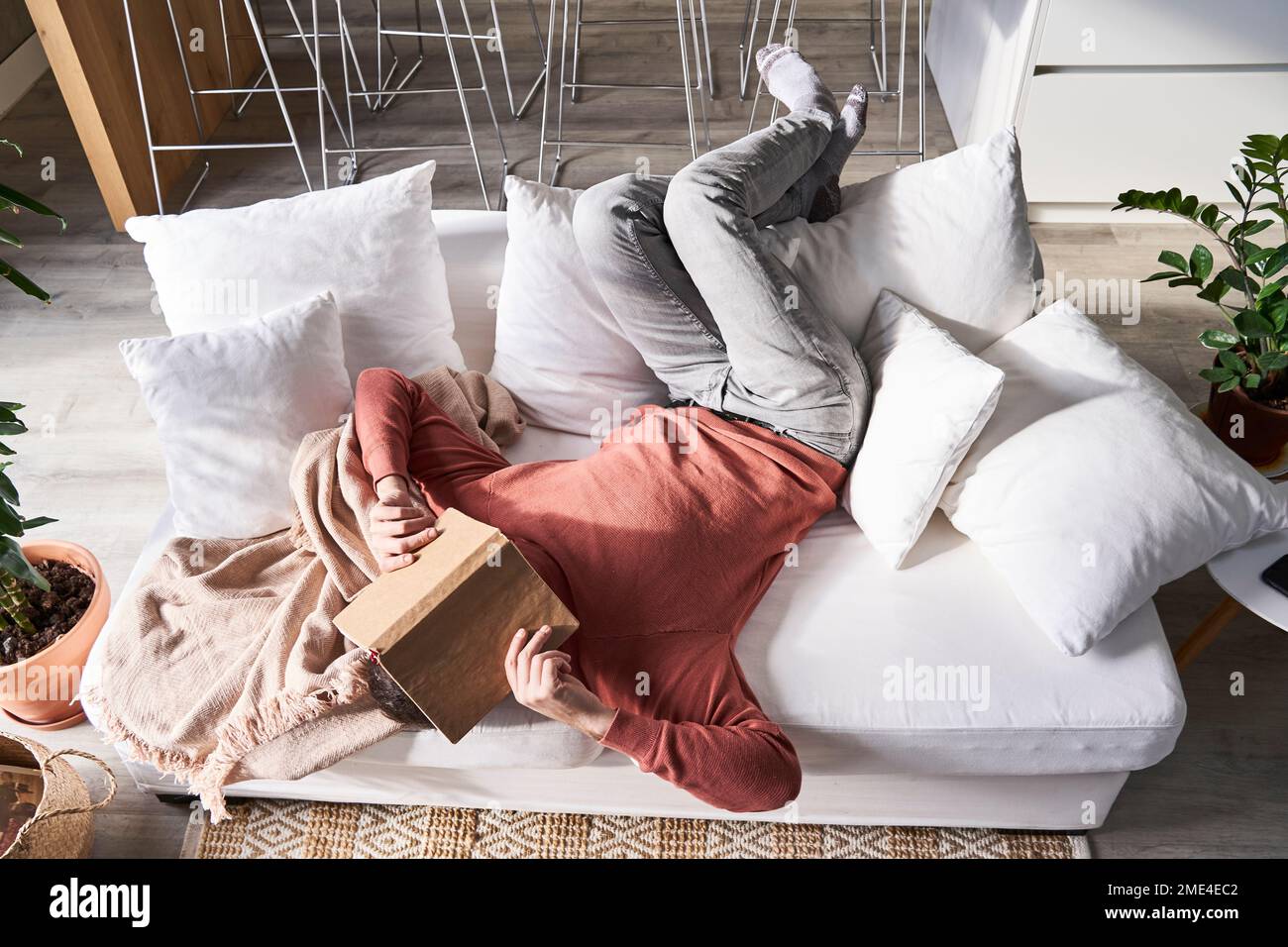 Man covering face with book lying on sofa at home Stock Photo - Alamy