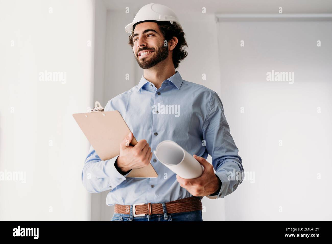 Happy engineer wearing hardhat holding blueprints in office Stock Photo ...