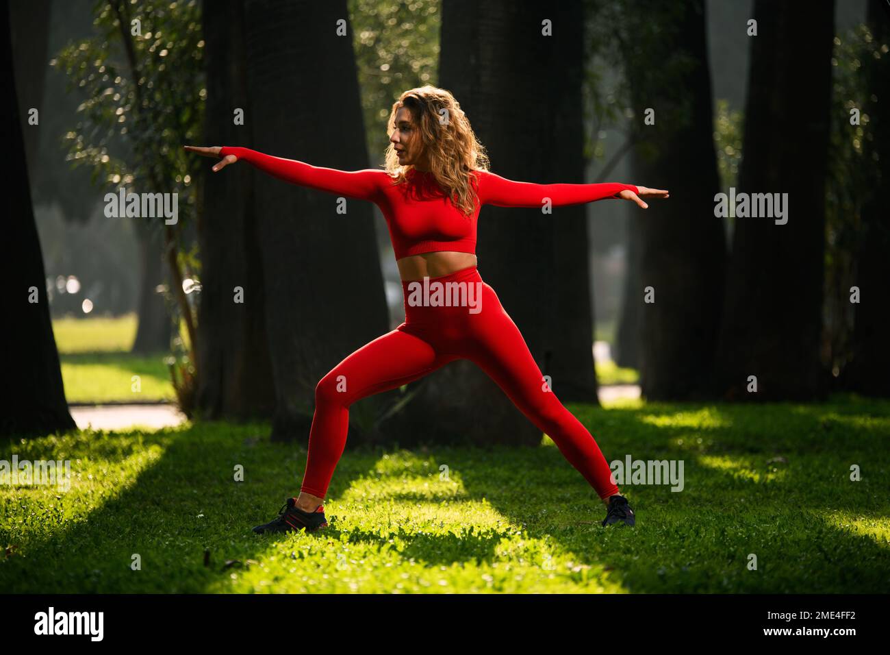 Woman with red colored yoga dress, posing yoga movements on a green ...
