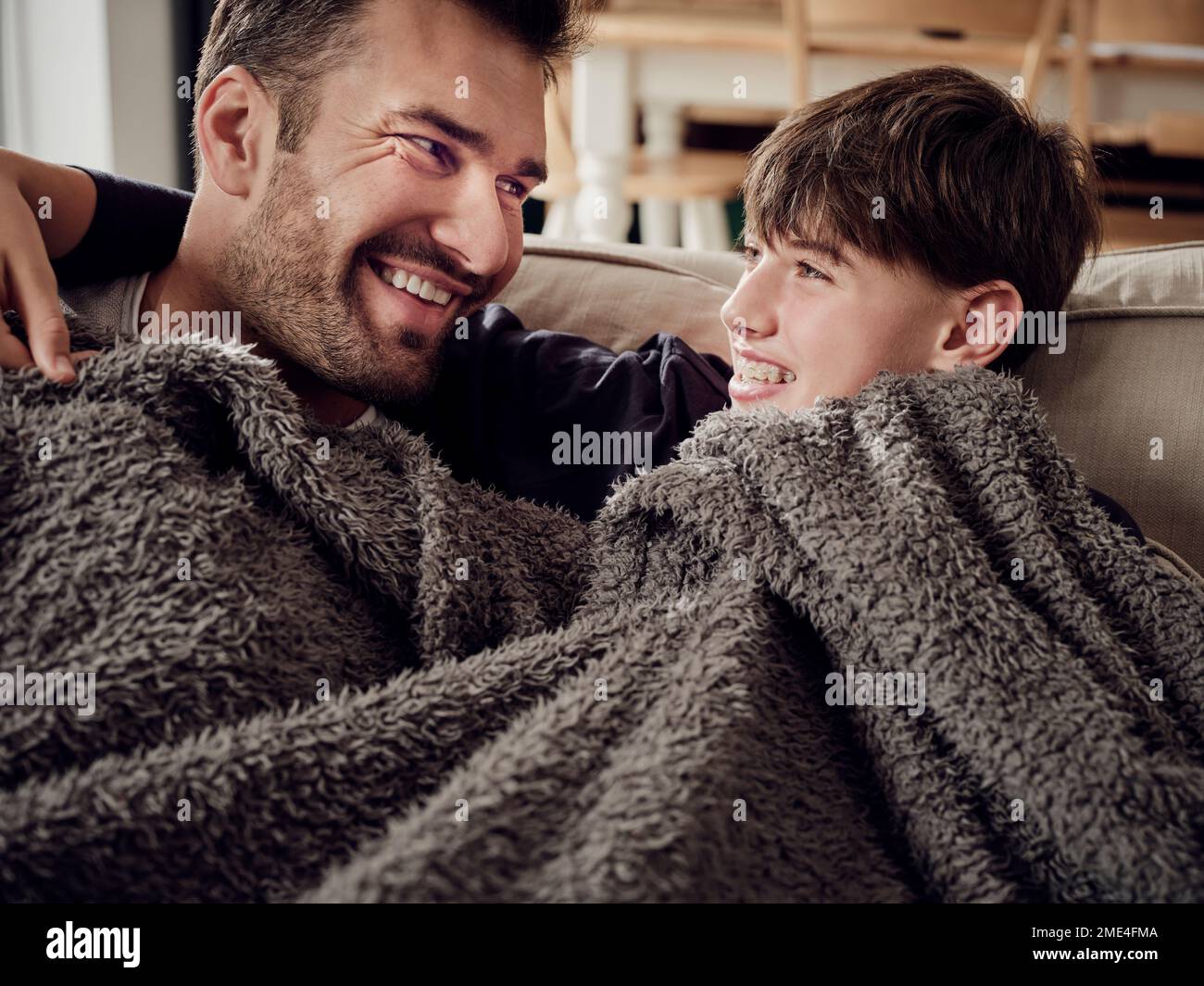 Father son snuggling under a blanket couch living room hi-res stock ...