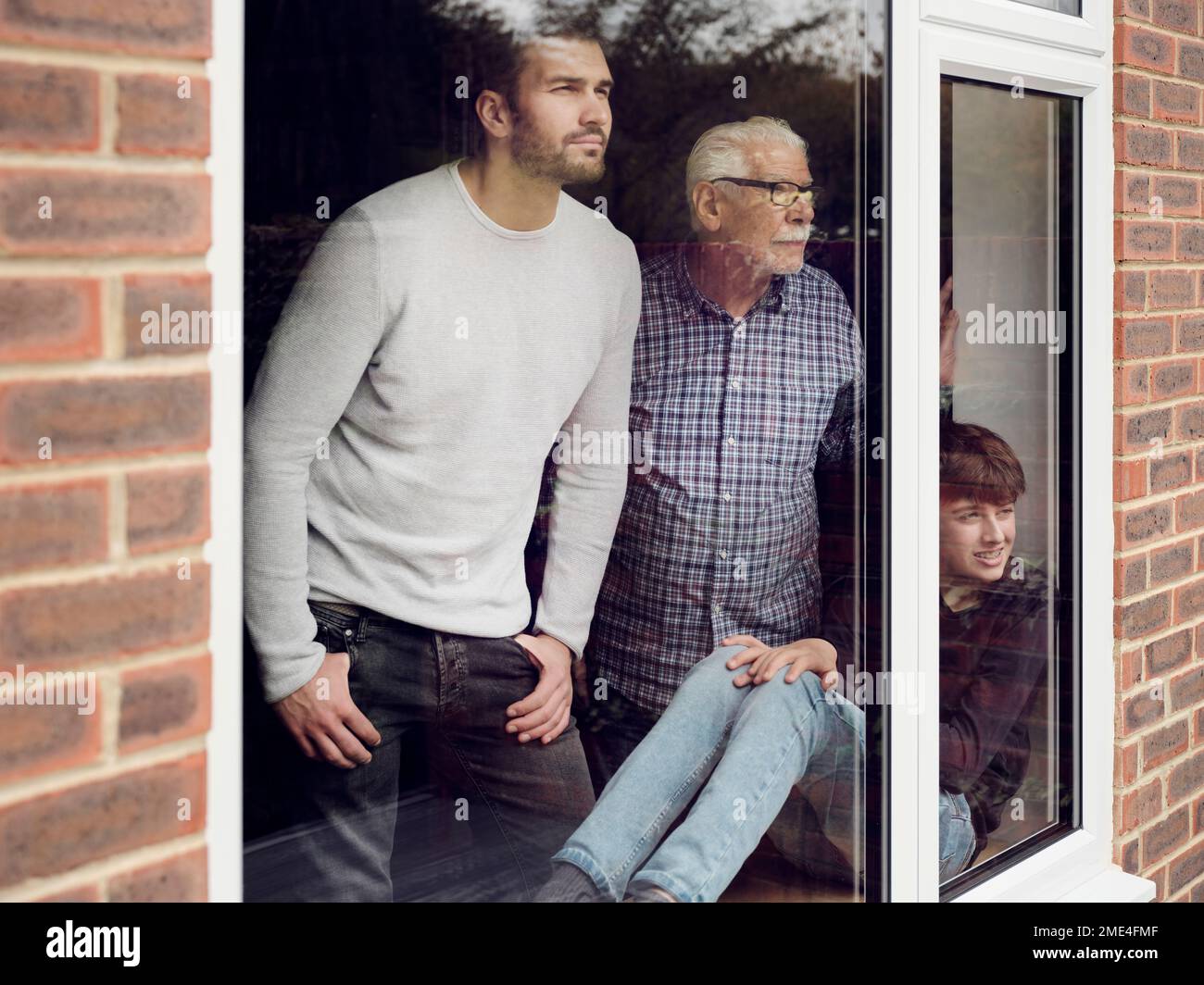Grandfather, father and son looking out of the window at home Stock ...