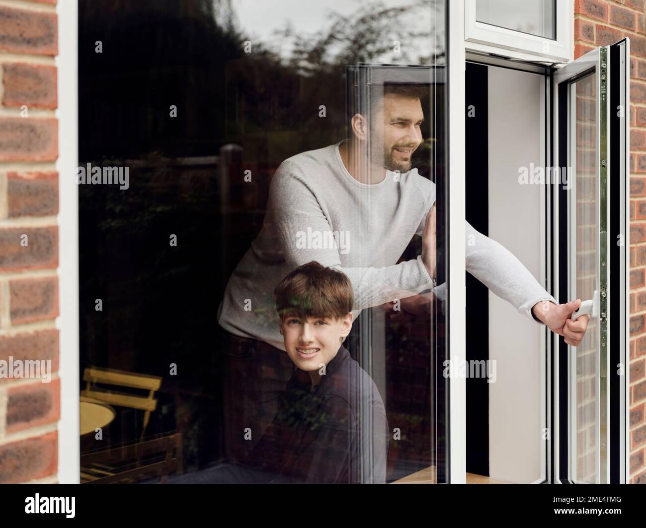 Man with son looking out and closing the window at home Stock Photo - Alamy