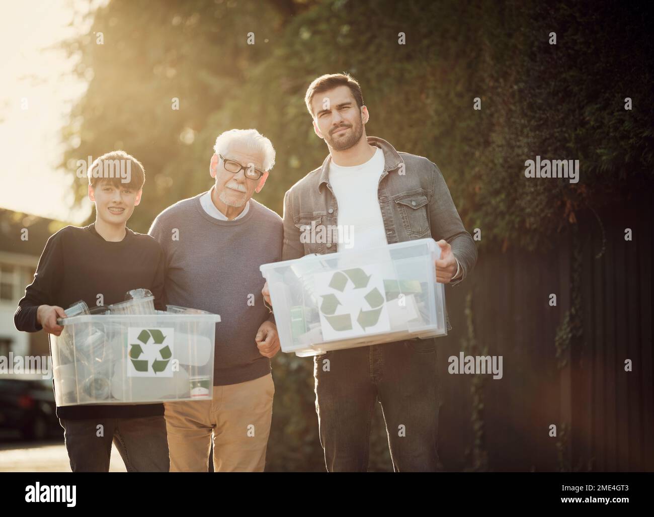 Grandfarher, father and son standing outdoors carrying recycling boxes ...