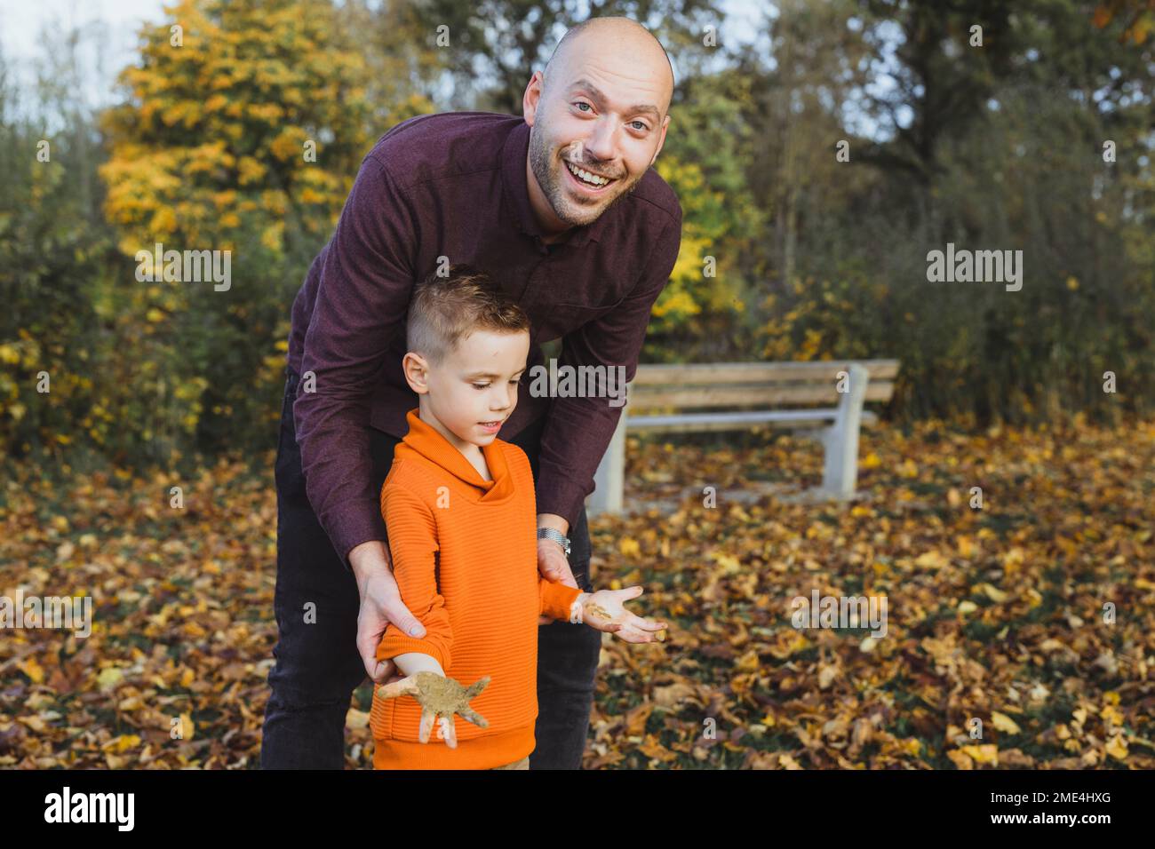 Father laughing and holding hands of son smeared with sand in autumn ...