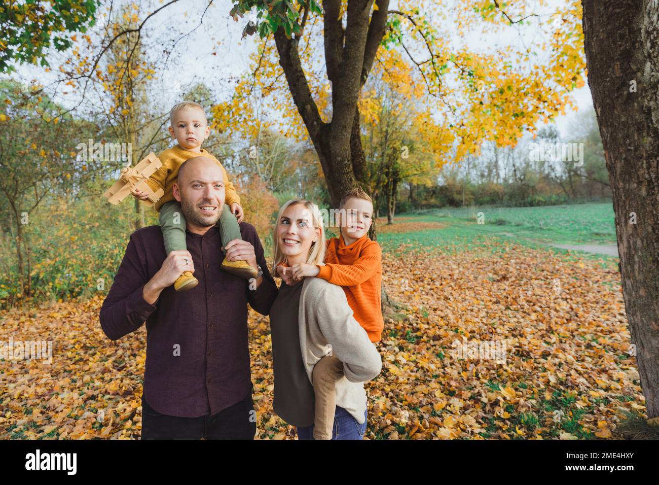 Parents giving piggyback ride to children in autumn forest Stock Photo ...