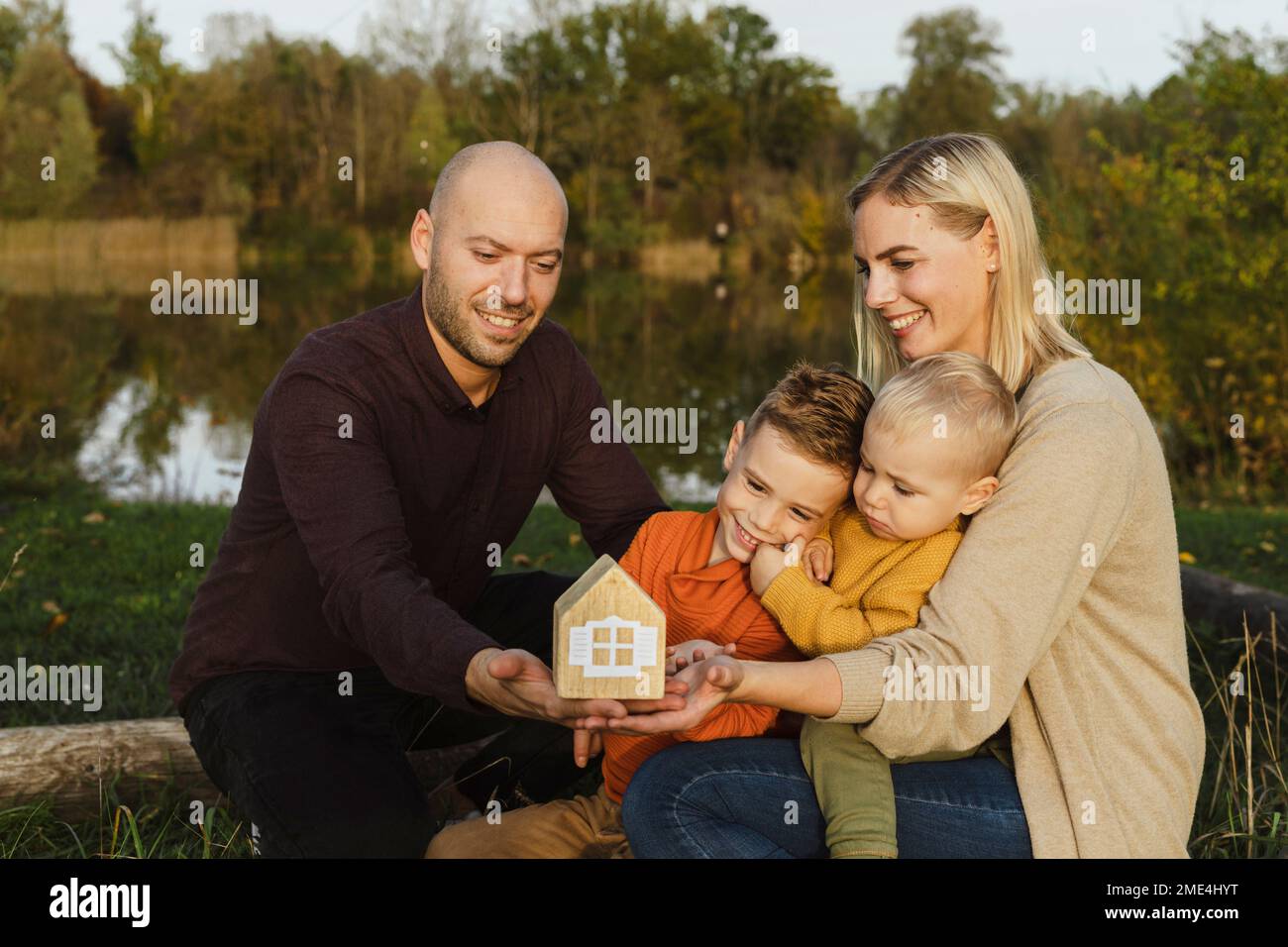 Smiling parents with children holding wooden model house in nature ...